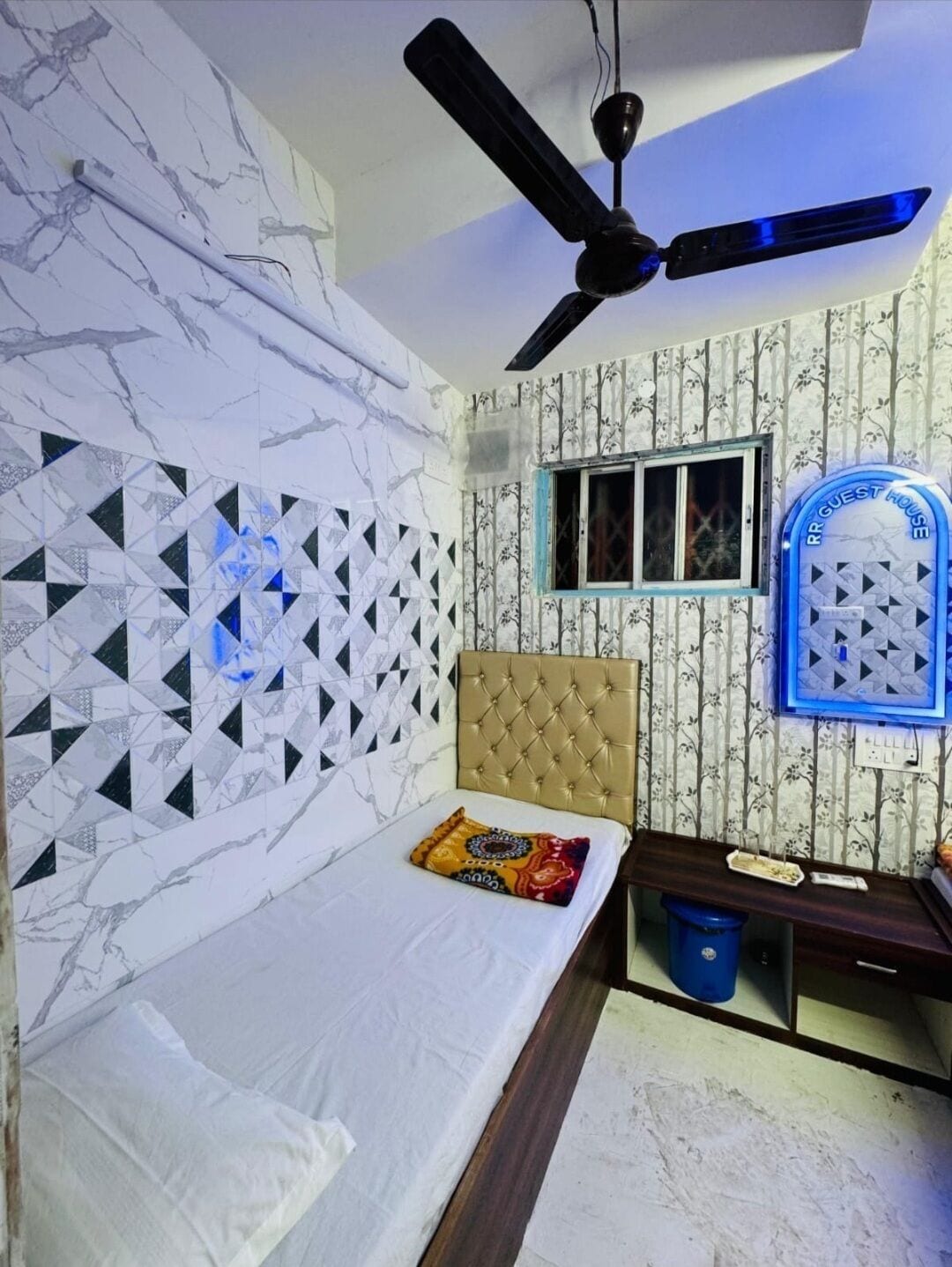 Quarto com cama, ventoinha no teto, janela e televisão fixada na parede.