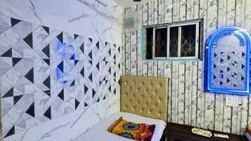 Quarto com cama, ventoinha no teto, janela e televisão fixada na parede.