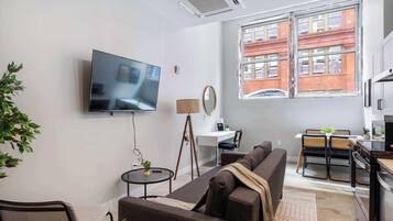 Uma sala de estar moderna com televisão de tela plana, um sofá, uma área de jantar com mesa e cadeiras, e uma cozinha com fogão.