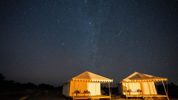 Duas tendas numa praia de areia sob um céu estrelado.