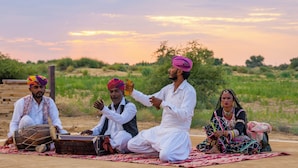 Um grupo de pessoas sentadas em um cobertor ao ar livre, tocando instrumentos musicais tradicionais.