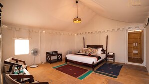 Quarto com cama, mesas de cabeceira, escrivaninha, cadeira, ventilador e janela.