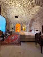 Quarto com teto de pedra, cama, tapete vermelho e mesa com cadeiras.