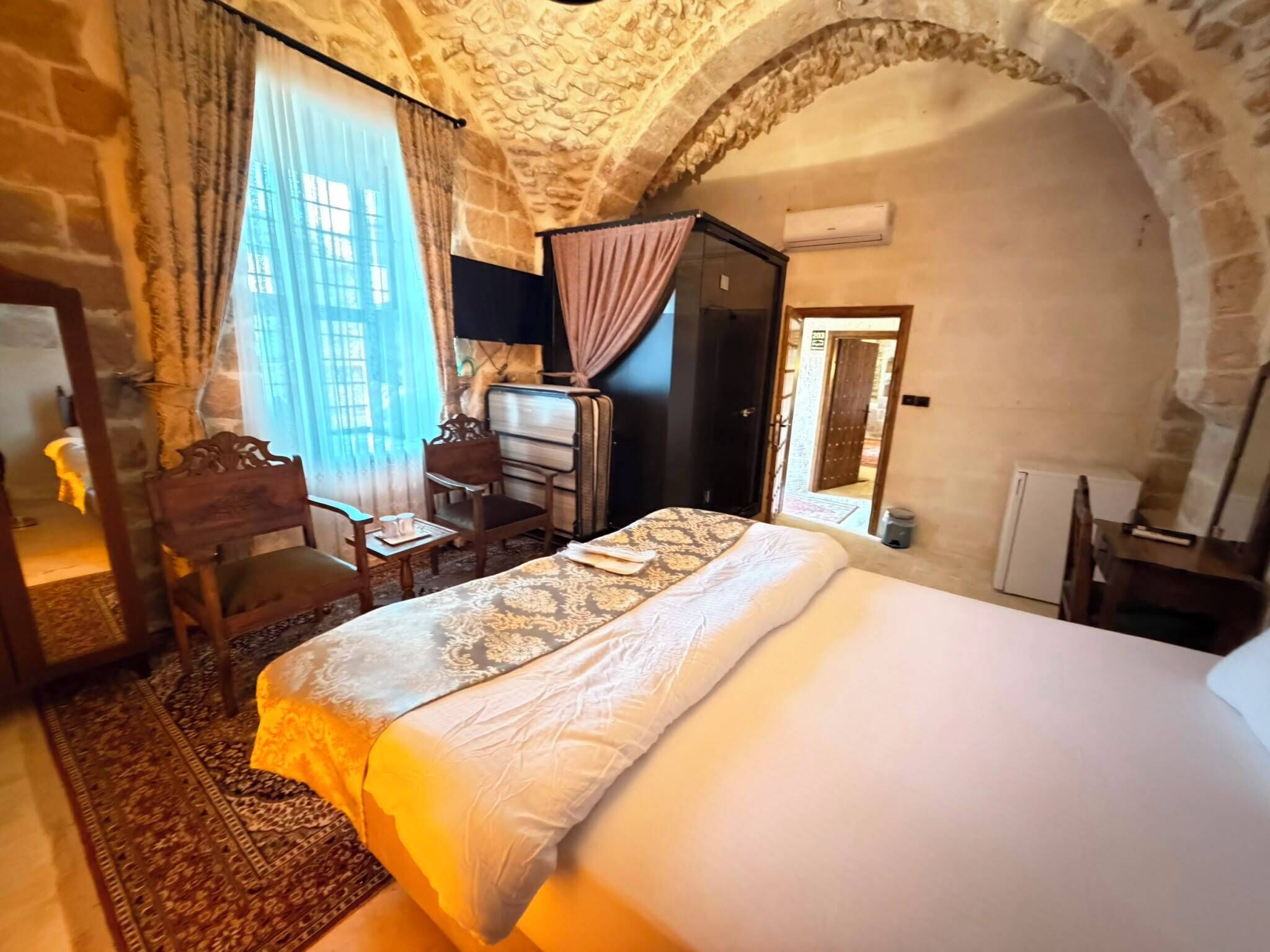 Quarto de hotel com uma cama grande, escrivaninha, cadeira e guarda-roupa.