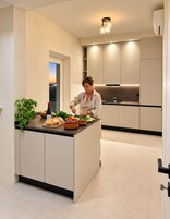 Cozinha moderna com ilha central, uma pessoa preparando comida e vista para o pôr do sol pela janela.