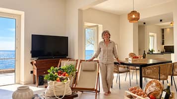 Uma sala ampla com televisão, mesa de jantar e cadeiras. Uma mulher atravessa o espaço.