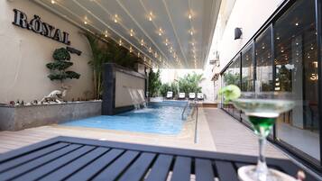 Área de piscina no terraço com uma placa indicando 'ROYAL regency' e um espaço de bar com um copo de martini.