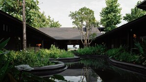Um jardim tranquilo com um espelho d'água, rodeado por vegetação exuberante e árvores.