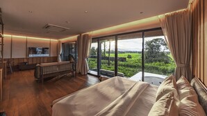 Quarto com cama grande, vista para o campo, um pequeno espaço de estar e televisão.