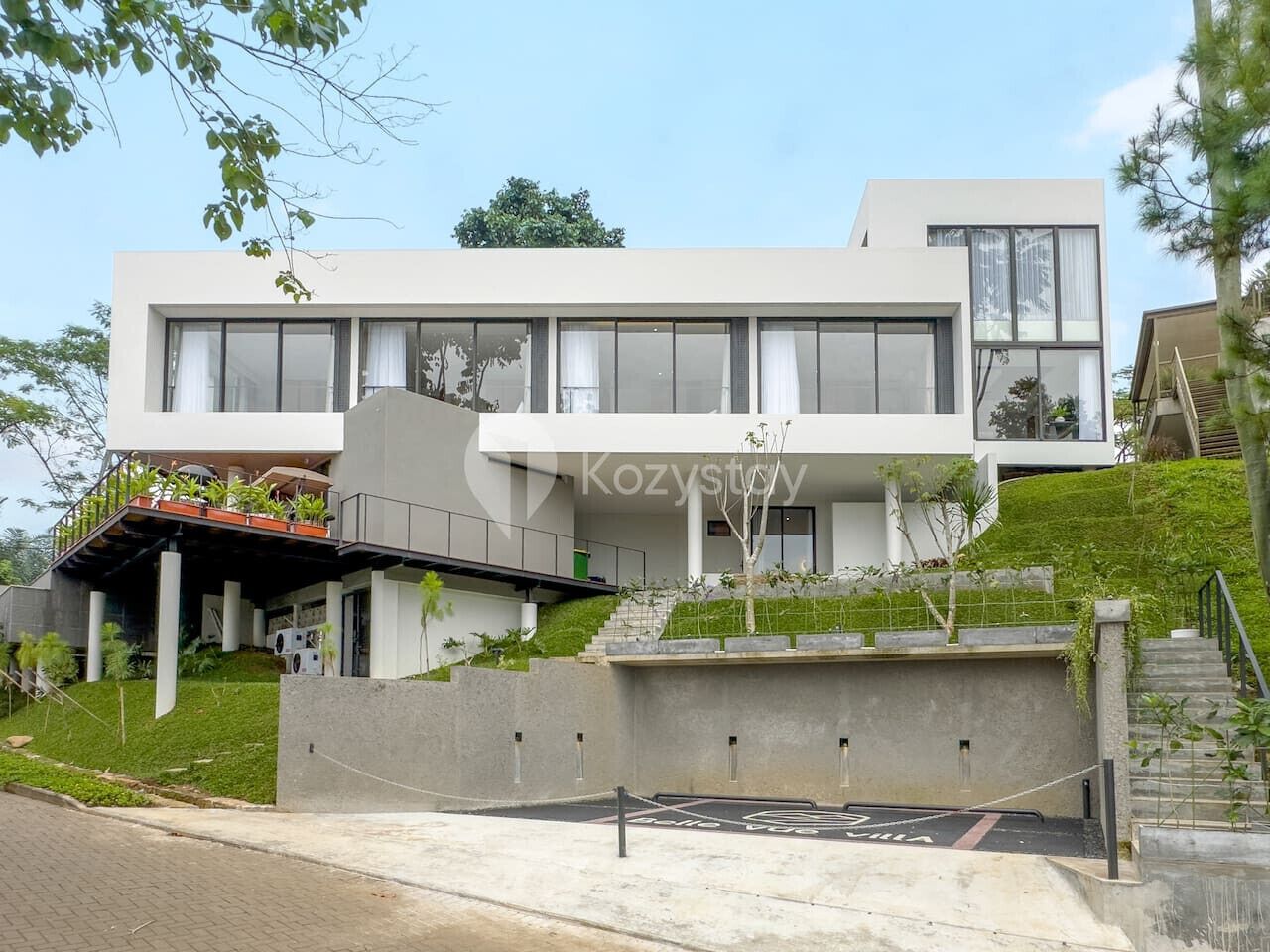 Um edifício moderno de dois andares com grandes janelas, entrada coberta e área ajardinada com escadas.