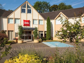 Um hotel com um destaque para a placa vermelha da Ibis, uma piscina e um jardim ajardinado.
