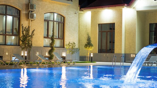 Piscina com cascata, espreguiçadeiras e um edifício com grandes janelas e aparelhos de ar condicionado.