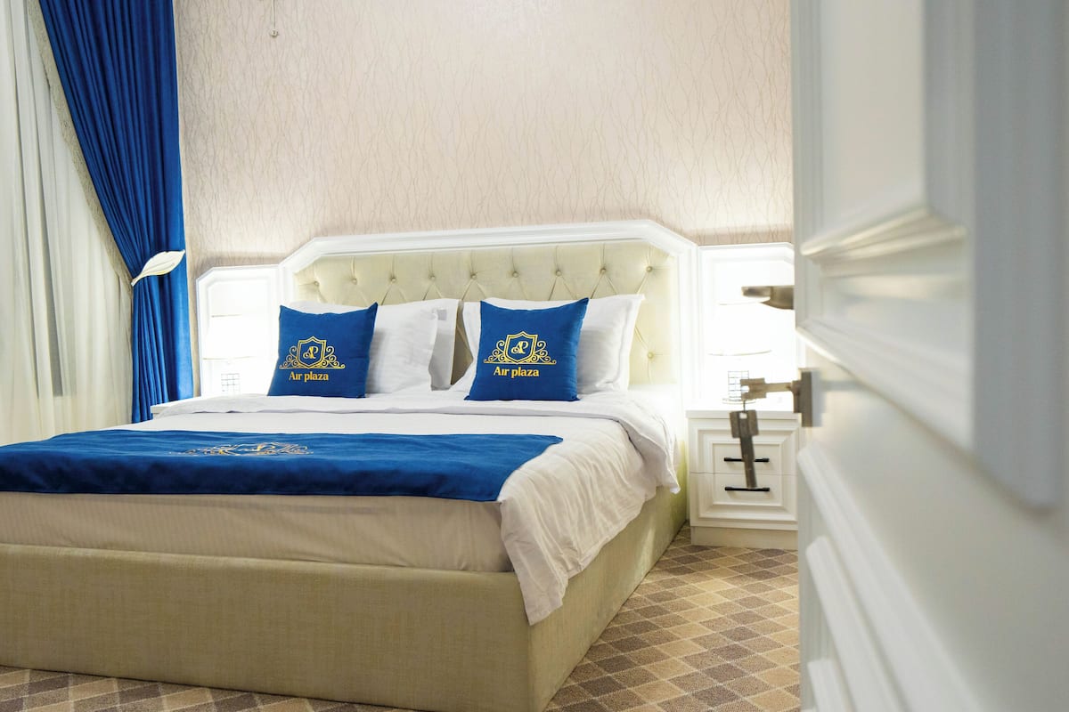 Cama bem arrumada com cabeceira branca, roupa de cama azul e almofadas combinando.