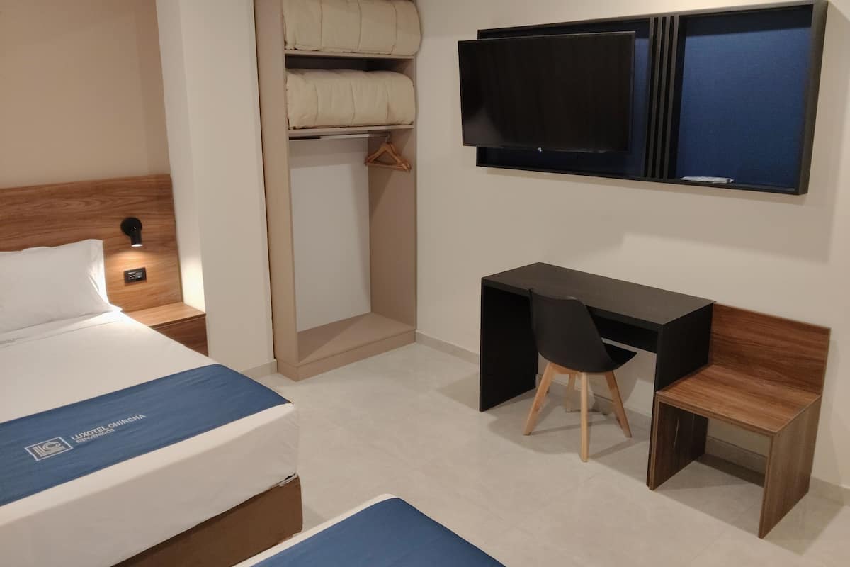 Quarto de hotel com cama, secretária, cadeira, televisão e guarda-roupa.