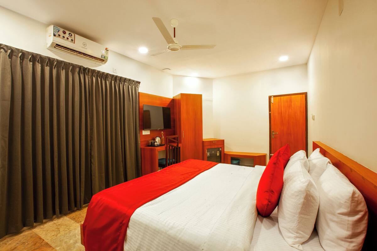 Quarto de hotel com cama, escrivaninha, cadeira, televisão e guarda-roupa.
