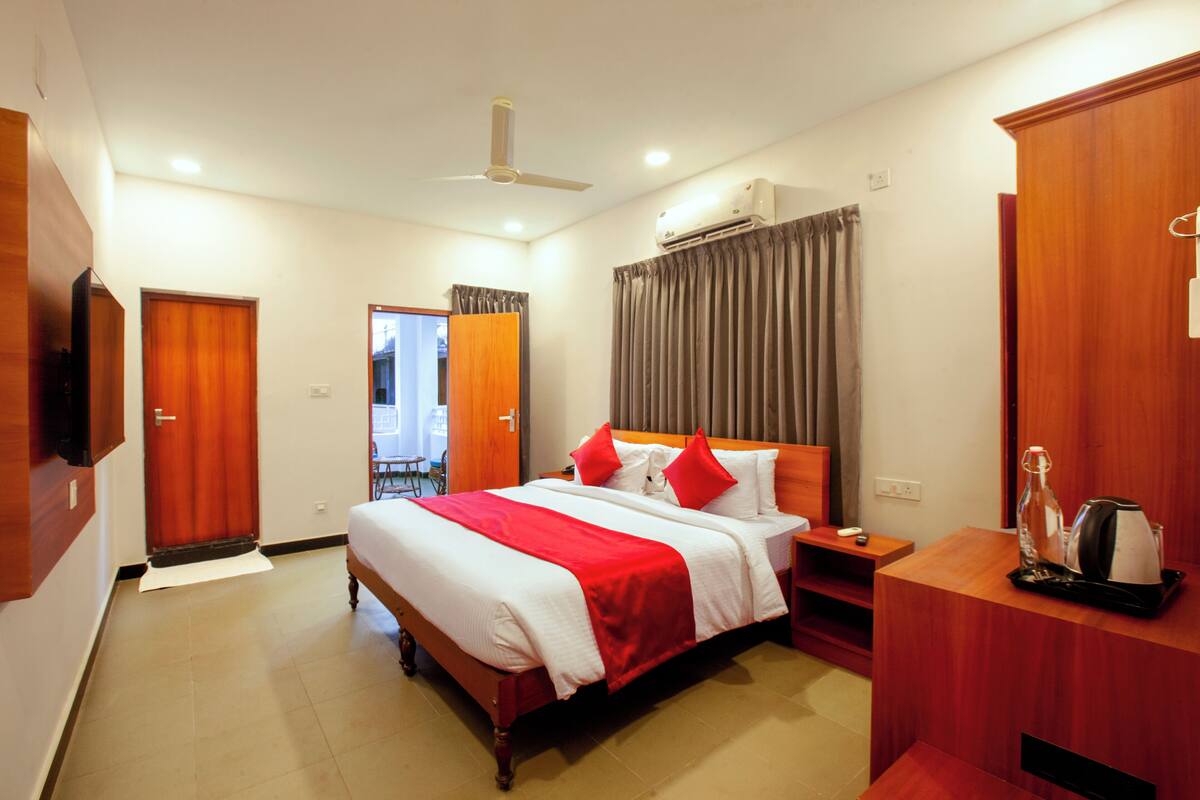 Quarto de hotel com cama, escrivaninha, guarda-roupa e ar condicionado.
