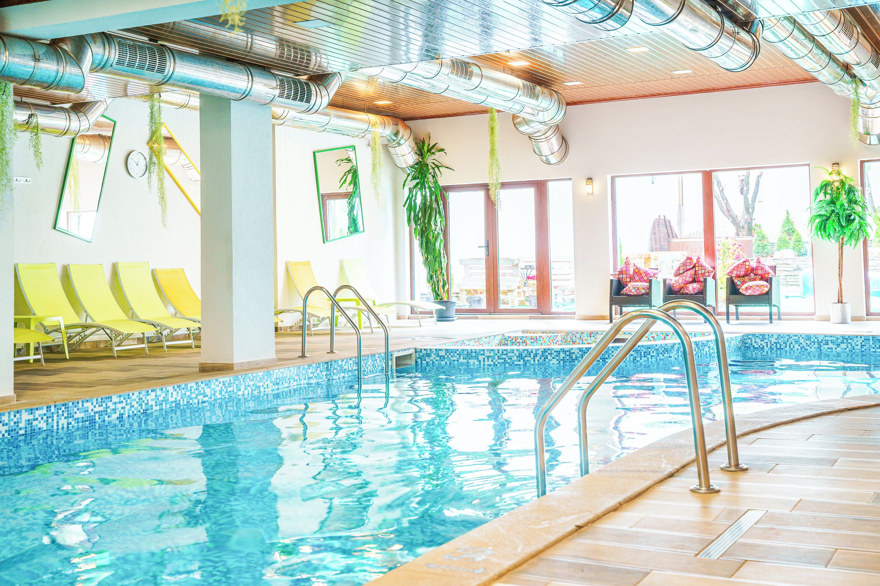 Uma piscina interna com água cristalina, cadeiras de descanso amarelas e plantas em vasos.