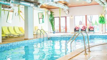 Uma piscina interna com água cristalina, cadeiras de descanso amarelas e plantas em vasos.