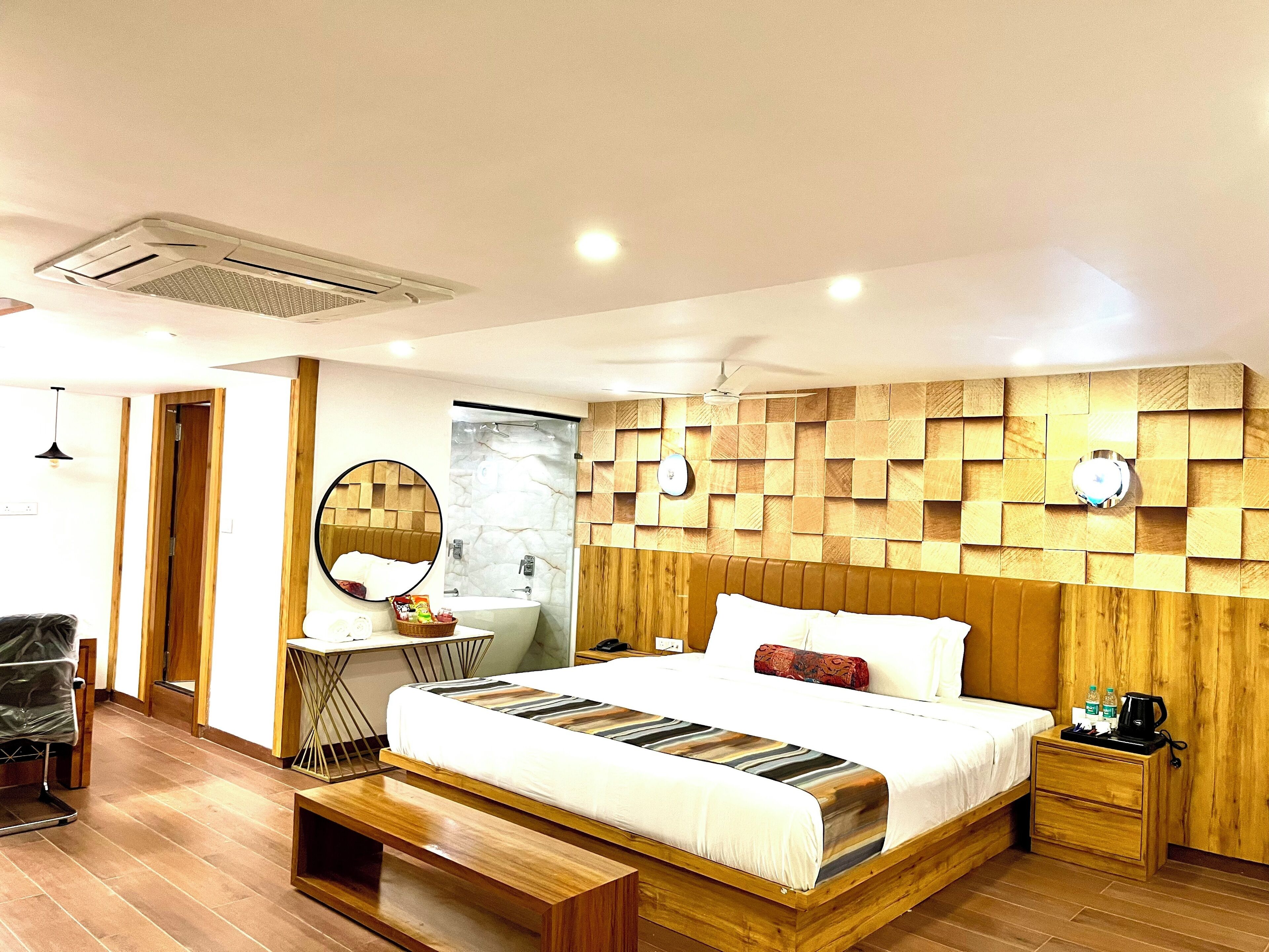 Um quarto moderno com cabeceira de madeira, uma cama grande, uma mesinha de cabeceira e um banheiro com espelho e pia.