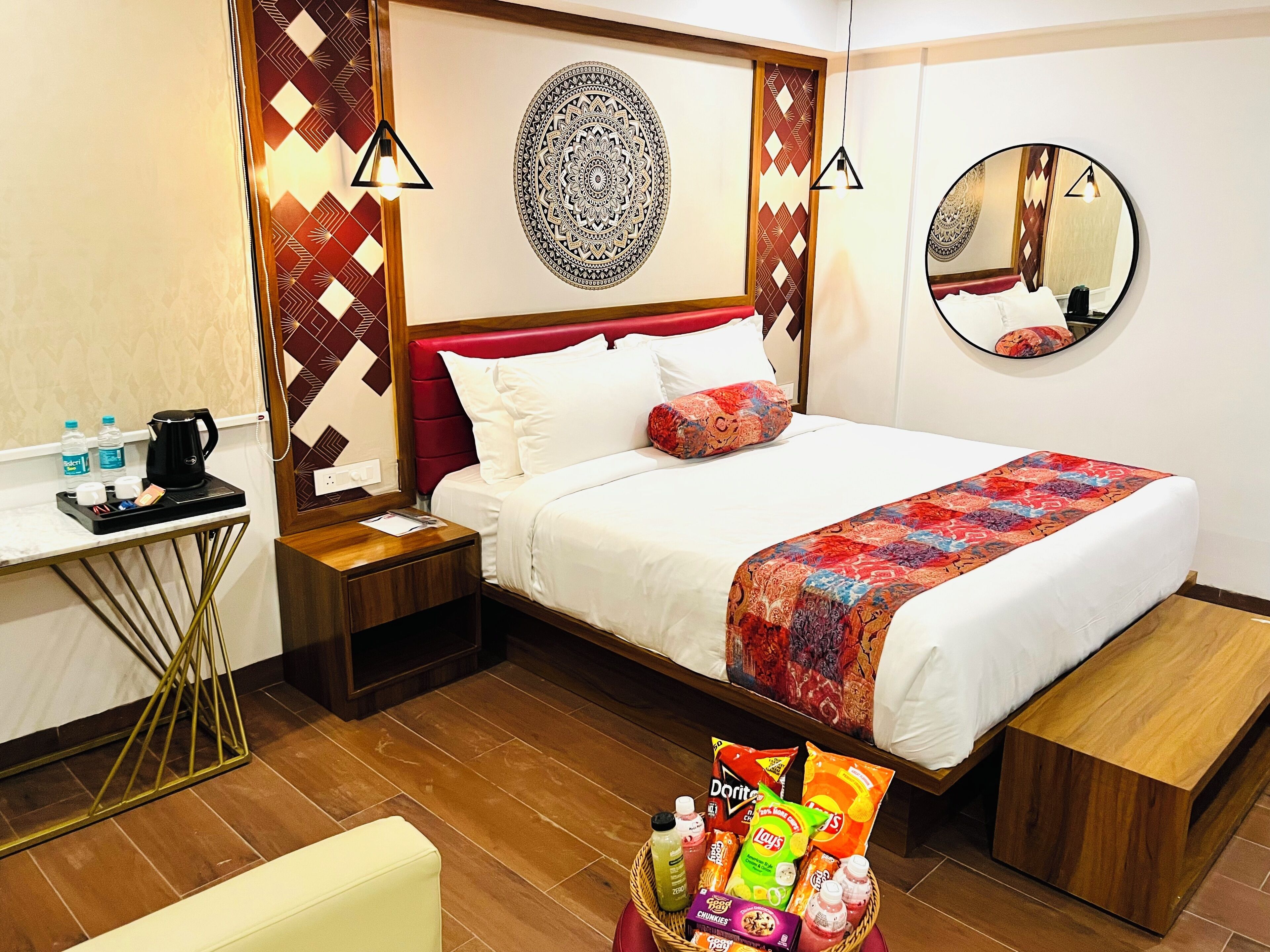Quarto de hotel com cama, mesa de cabeceira, espelho, parede com padrão decorativo e pequena mesa com lanches.