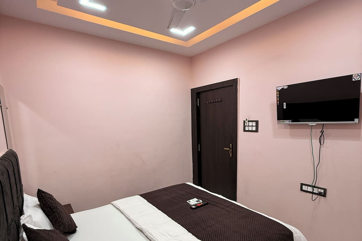 Quarto com cama, travesseiros, televisão, ventoinha no teto e uma porta.