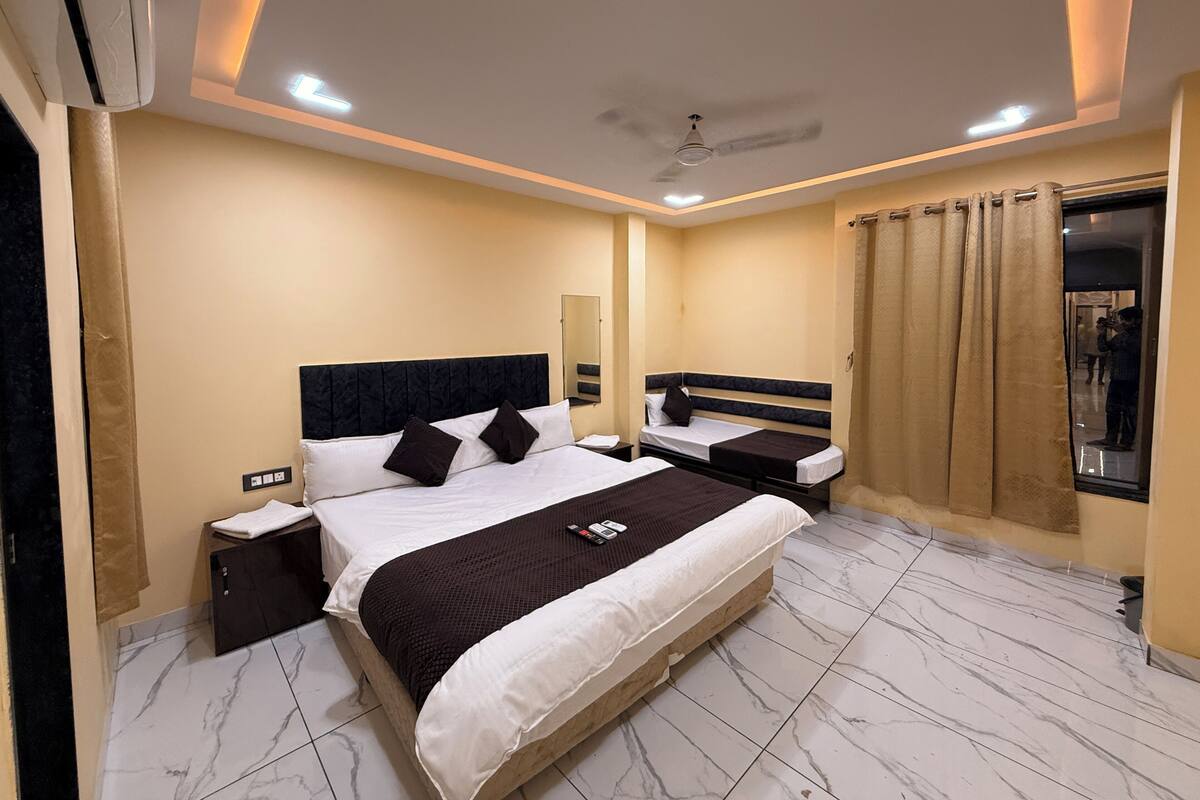 Quarto de hotel com uma cama grande, duas mesas de cabeceira, um ventilador de teto e uma janela com cortinas.