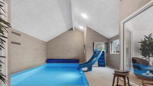 Piscina interna com um escorrega azul, um espaço de estar pequeno e vista para o exterior.