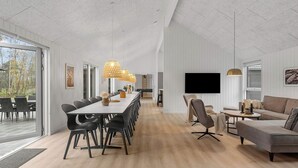Um quarto amplo com uma mesa de jantar comprida, cadeiras modernas, um sofá e uma televisão.