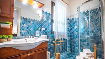 Casa de banho com toucador de madeira, lavatório e espelho. Existe uma área de duche com porta de vidro e azulejos azuis.
