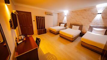 Quarto de hotel com duas camas, uma escrivaninha, uma cadeira, um guarda-roupa e um ar condicionado.