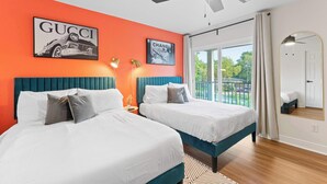 Quarto de hotel com duas camas, um ventilador de teto e uma janela grande com vista para área verde.