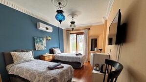 Quarto com duas camas, uma escrivaninha, uma cadeira, televisão e janela com cortinas.