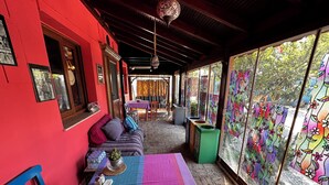 Quarto aconchegante com parede vermelha, sofá estampado, mesa com toalha colorida e janela com vitrais.