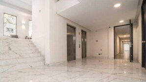 Um corredor amplo com piso de mármore, uma escadaria e dois elevadores.