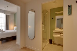 Quarto de hotel com cama, espelho grande, chuveiro e banheiro com pia e espelho.