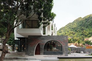 Um edifício moderno com fachada de pedra, grandes janelas e área de piscina.