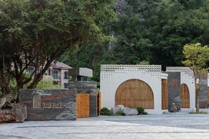 Um edifício moderno com fachada de pedra, grandes portas de madeira e uma placa com a inscrição 'ONE DAY TANGKUS DISTRICT'.