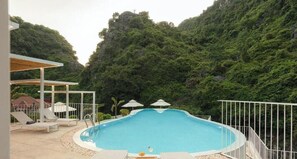Piscina cercada por uma grade branca, com espreguiçadeiras e guarda-sóis.