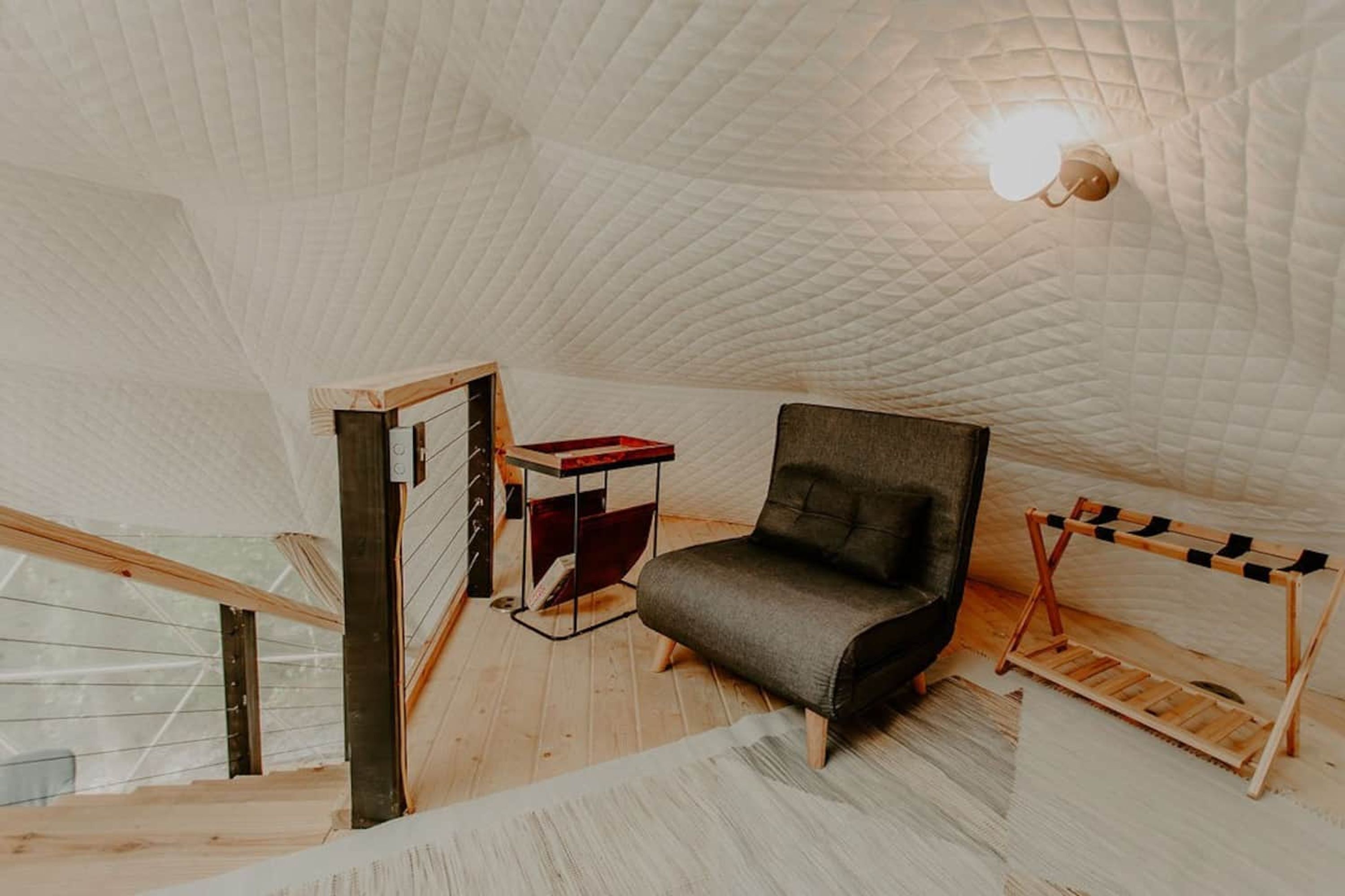 Quarto aconchegante e compacto, com cadeira estofada, mesa pequena e banco de madeira.