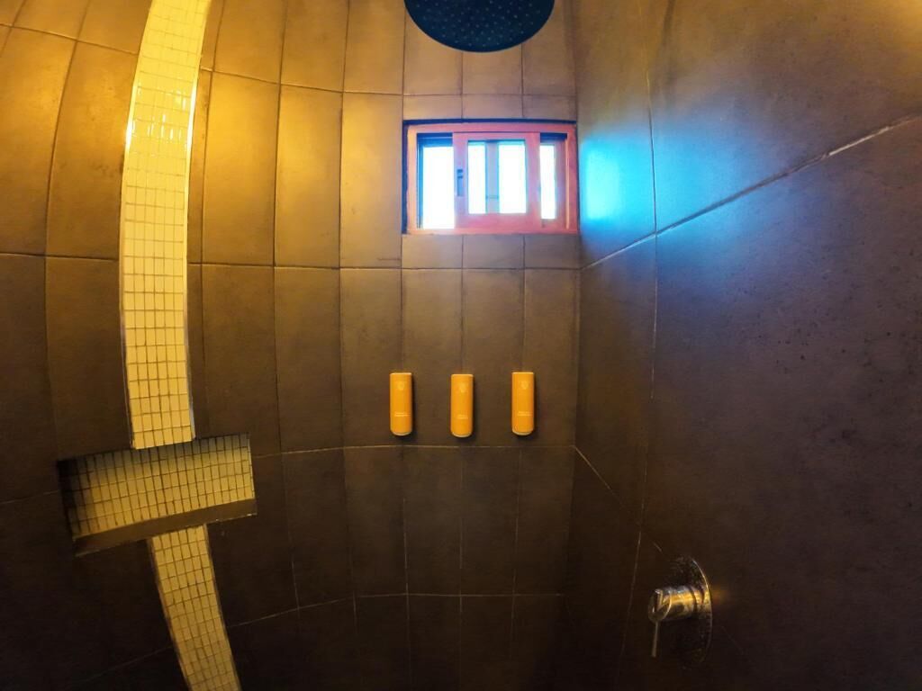 Casa de banho com parede azulejada, uma pequena janela e três dispensadores amarelos.