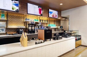 Interior de uma cafeteria com balcão, máquinas de espresso, vitrine e quadro de cardápio.
