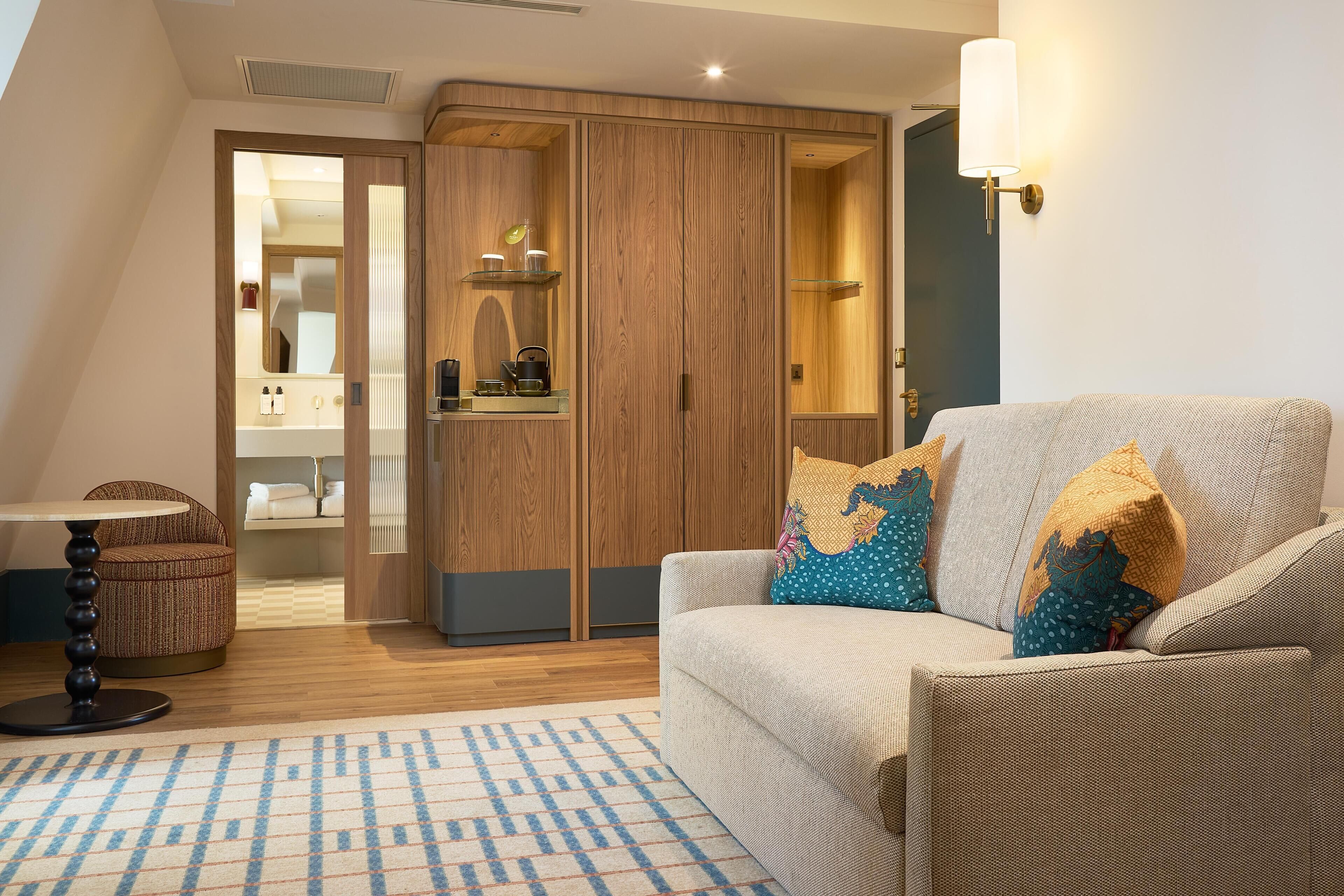 Um quarto com sofá, mesa redonda, tapete estampado, guarda-roupa e luminária fixada na parede.