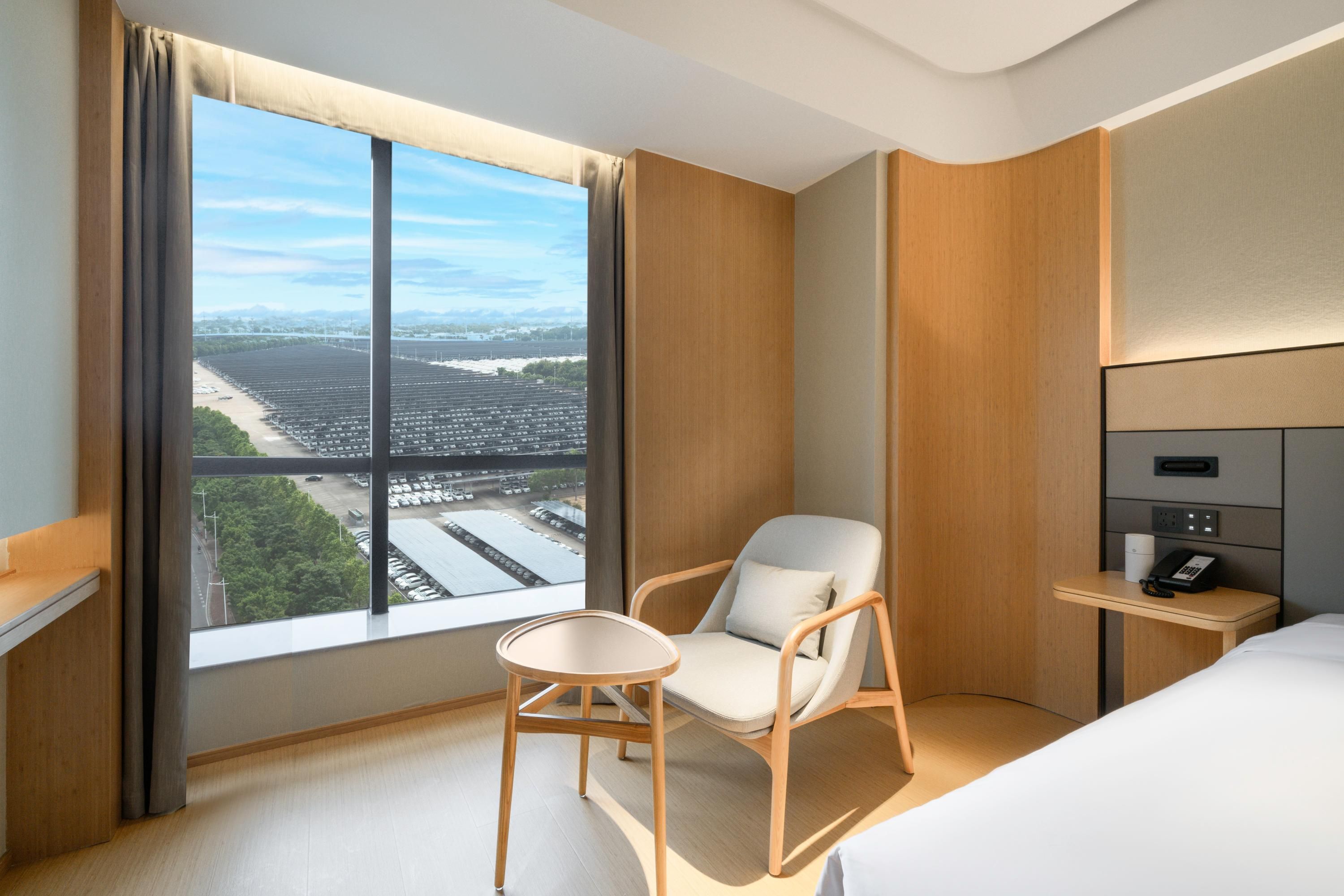 Quarto de hotel com uma janela grande, uma cadeira, uma mesa de cabeceira com telefone e uma cama.