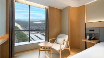 Quarto de hotel com uma janela grande, uma cadeira, uma mesa de cabeceira com telefone e uma cama.