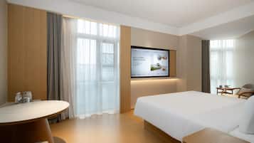 Quarto de hotel com cama, escrivaninha, TV fixada na parede e janela com cortinas.