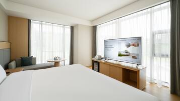 Quarto de hotel com uma cama grande, uma televisão sobre um suporte de madeira, uma mesinha com xícara e pires, e um sofá.