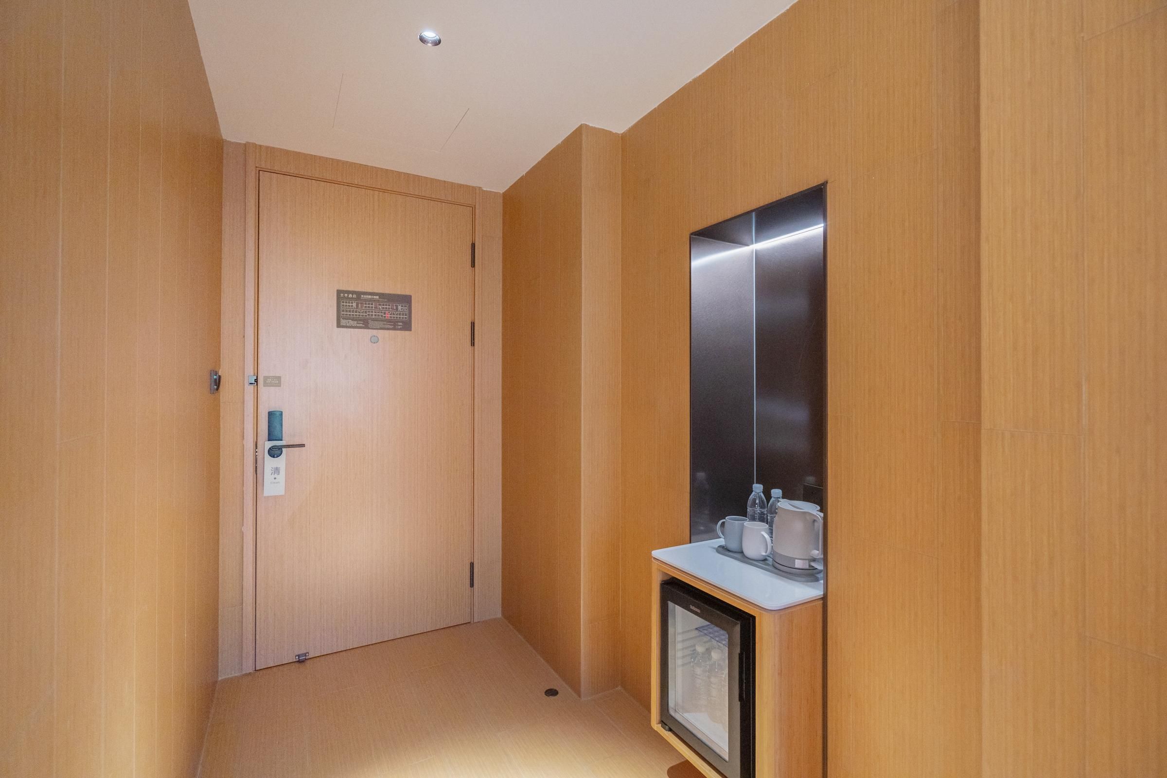 Um corredor com paredes de madeira, uma porta com uma placa e um balcão pequeno com um espelho e um quadro emoldurado.