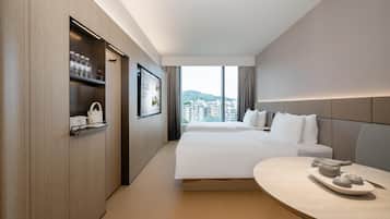 Quarto de hotel moderno com uma cama grande, mesa de cabeceira com bandeja, guarda-roupa com prateleiras e uma janela ampla com vista para a cidade.