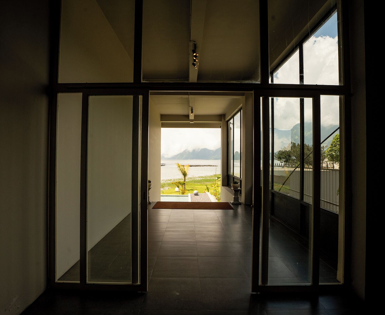 Corredor com grandes janelas que dão para um lago e montanhas.