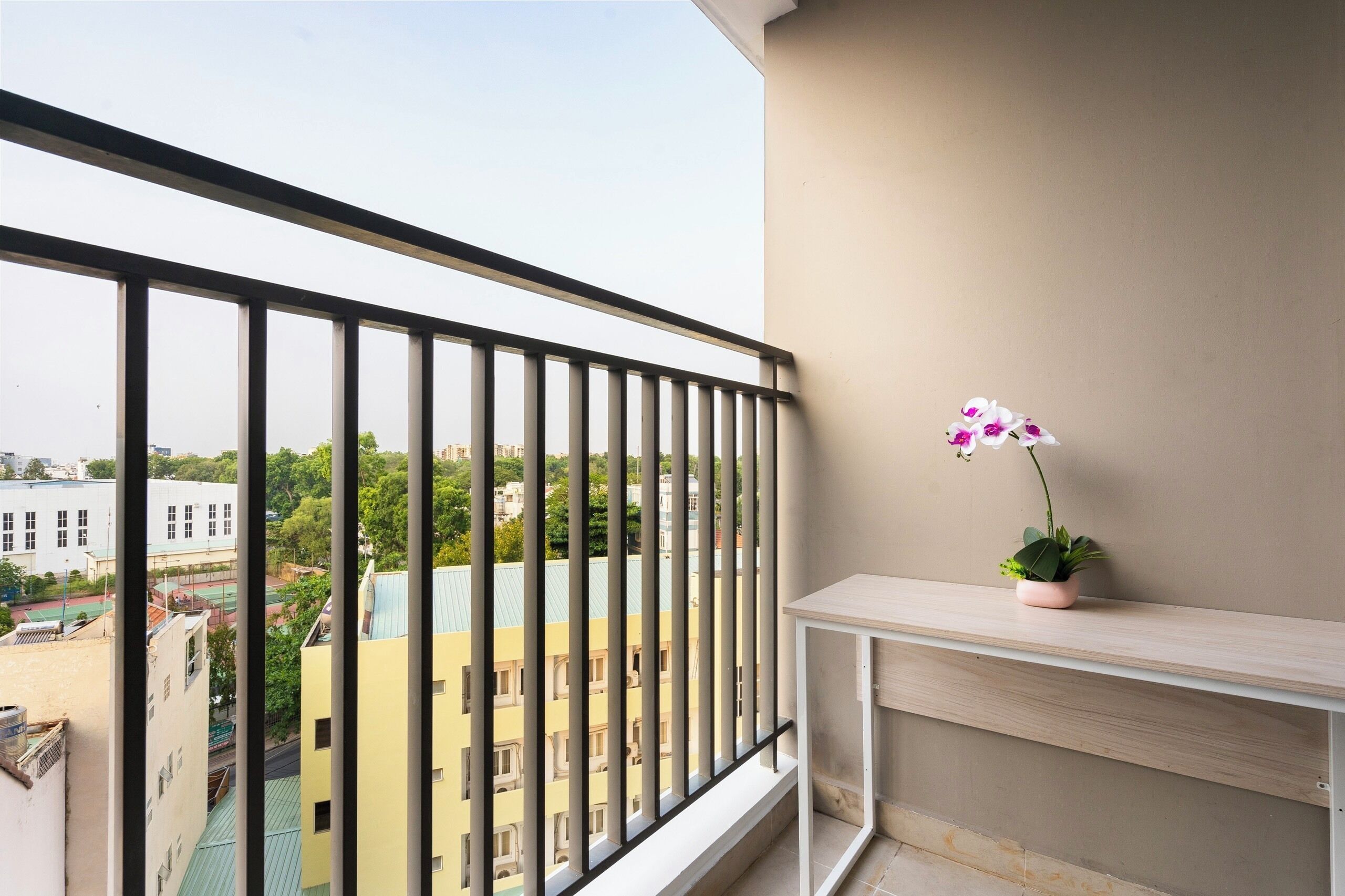 Varanda com grades de metal, uma orquídea em vaso e vista para edifícios e vegetação.